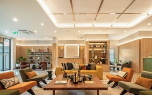 Um lobby moderno com área de estar central, balcão de recepção e estante com diversos objetos.