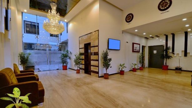 Um hall amplo com um candelabro, plantas em vasos e uma tela grande.