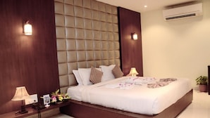 Quarto de hotel moderno com cama grande, cabeceira acolchoada, abajures, mesa de cabeceira e um vaso de planta.