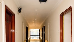 Um corredor longo e estreito, com chão de mármore e portas de madeira em ambos os lados.