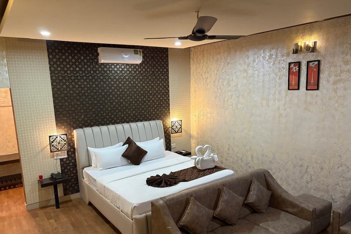 Quarto de hotel com cama, sofá, ventoinha no teto e luminárias fixadas na parede.