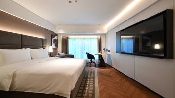 Quarto de hotel moderno com uma cama grande, uma escrivaninha, uma cadeira, uma televisão e uma janela com cortinas.
