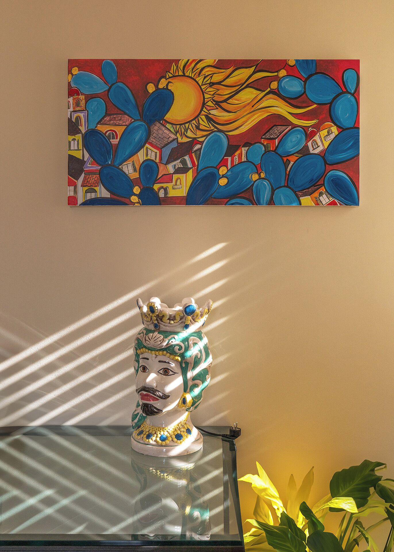 Uma estátua de cerâmica sobre uma mesa de vidro, com uma pintura colorida pendurada acima.