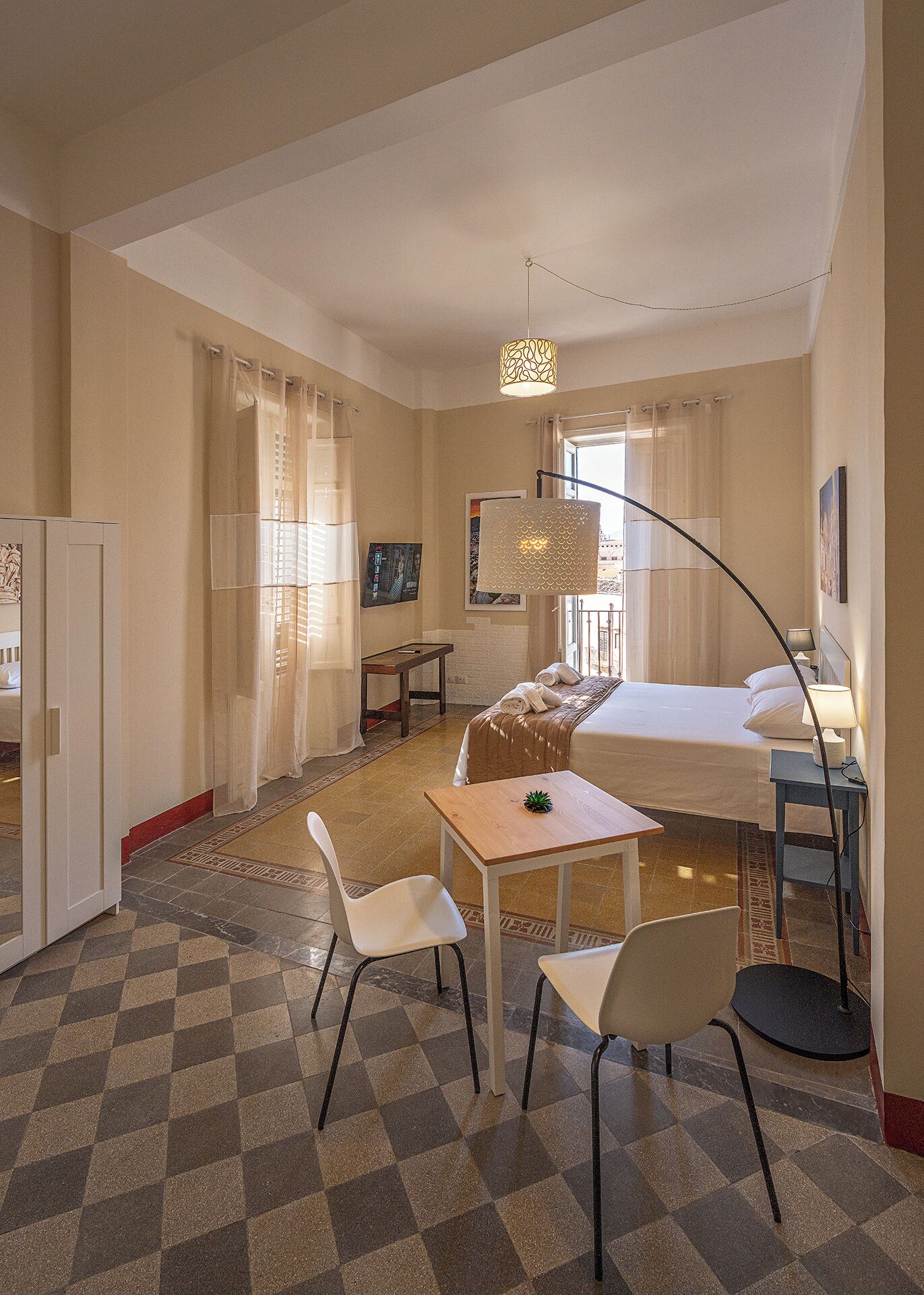 Quarto de hotel com cama, escrivaninha, cadeira, mesa e televisão.