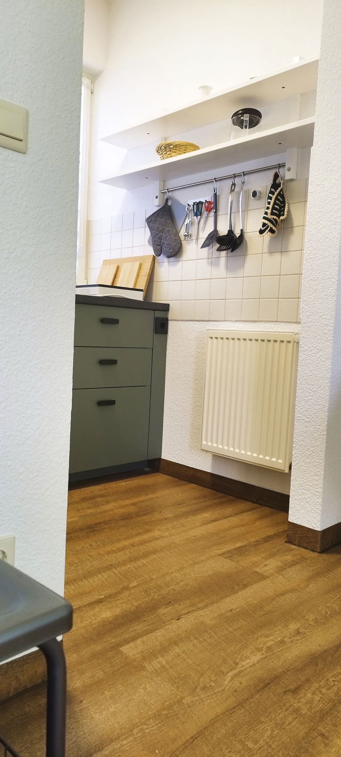 Uma cozinha com piso de madeira, bancada e um suporte na parede com utensílios de cozinha.