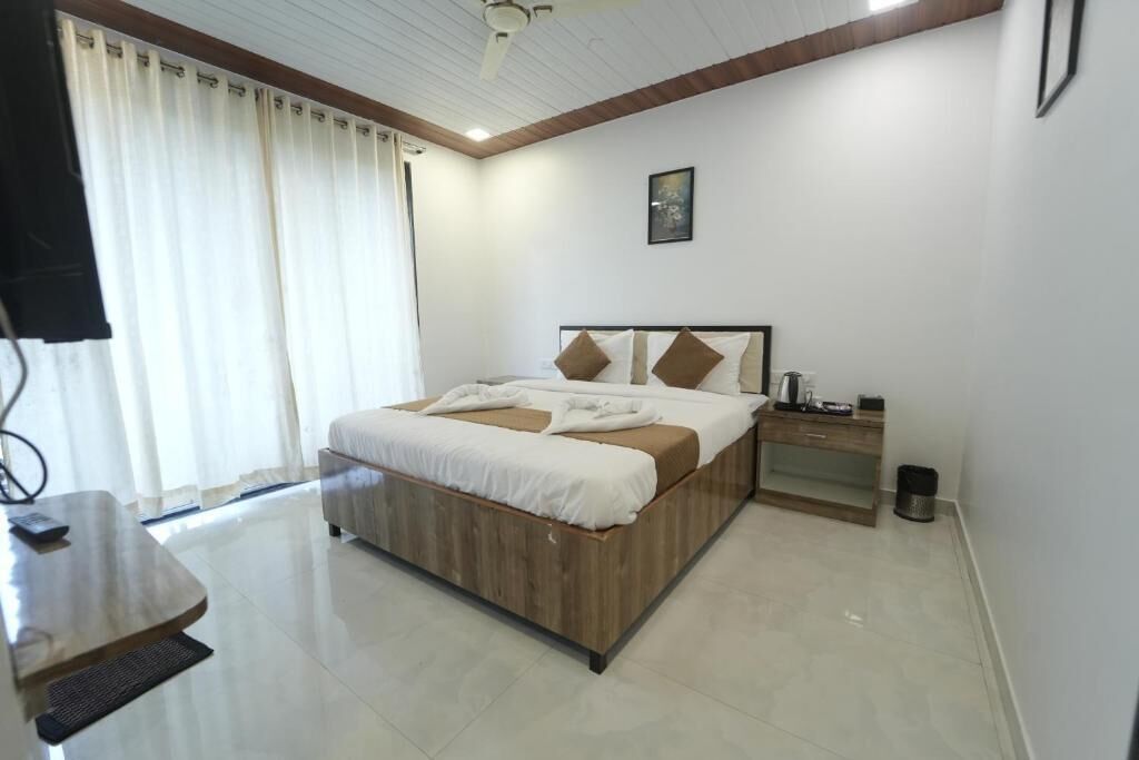 Quarto de hotel com cama de madeira, mesa de cabeceira, pequeno armário e ventoinha no teto.