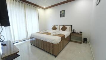 Quarto de hotel com cama de madeira, mesa de cabeceira, pequeno armário e ventoinha no teto.