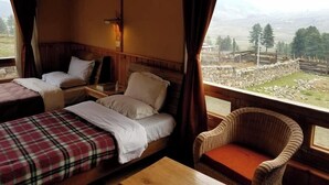 Um quarto de cabana acolhedor com duas camas, uma cadeira de vime e vista para uma paisagem montanhosa.