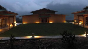 Um edifício com telhado plano e entrada central, rodeado por um gramado bem cuidado e caminhos.