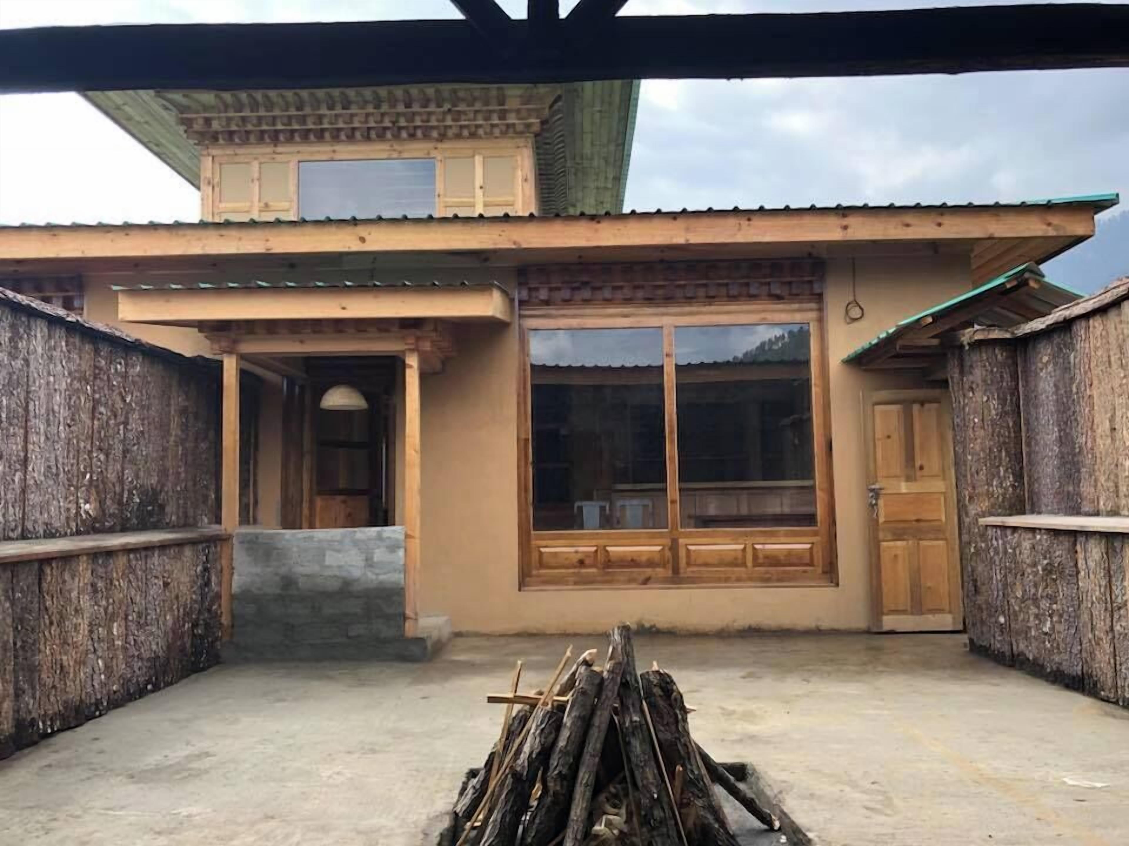 Uma casa de madeira tradicional com uma porta central e janelas, cercada por um pátio de concreto.
