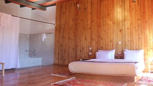 Quarto com parede de madeira, uma cama, banheiro com chuveiro e piso de madeira.