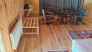 Quarto com piso de madeira, cama com colcha estampada, uma mesinha com chaleira e uma cadeira.