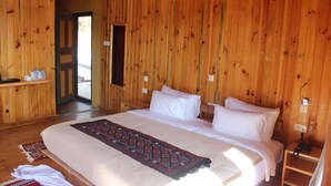 Um quarto com painéis de madeira, uma cama grande, uma mesinha de cabeceira e uma porta que dá para o exterior.