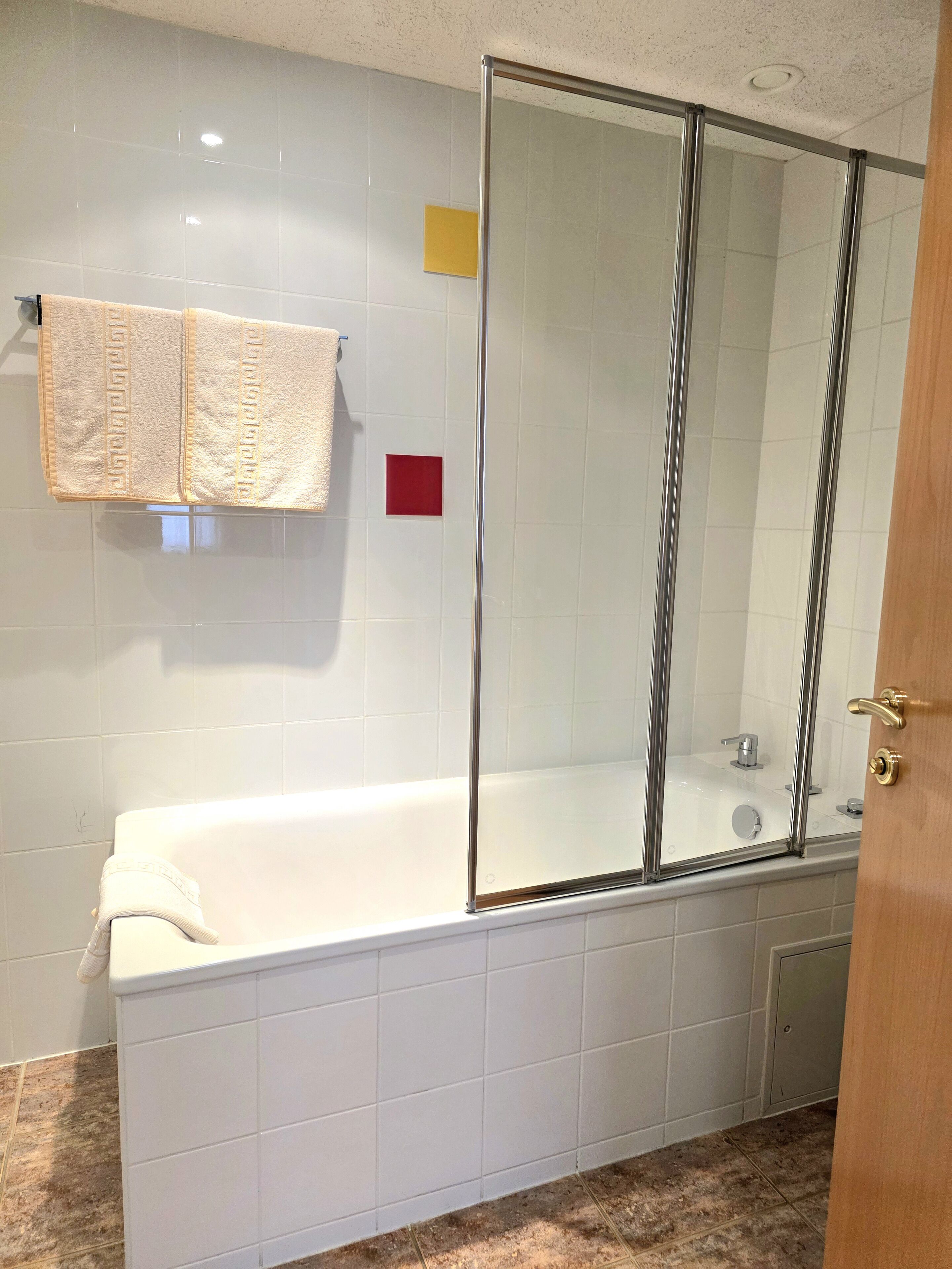 Um banheiro moderno com chuveiro envidraçado, banheira branca e porta-toalhas com toalhas estampadas.
