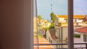 Visão pela janela de uma área residencial com edifícios, uma palmeira e uma placa de rua.