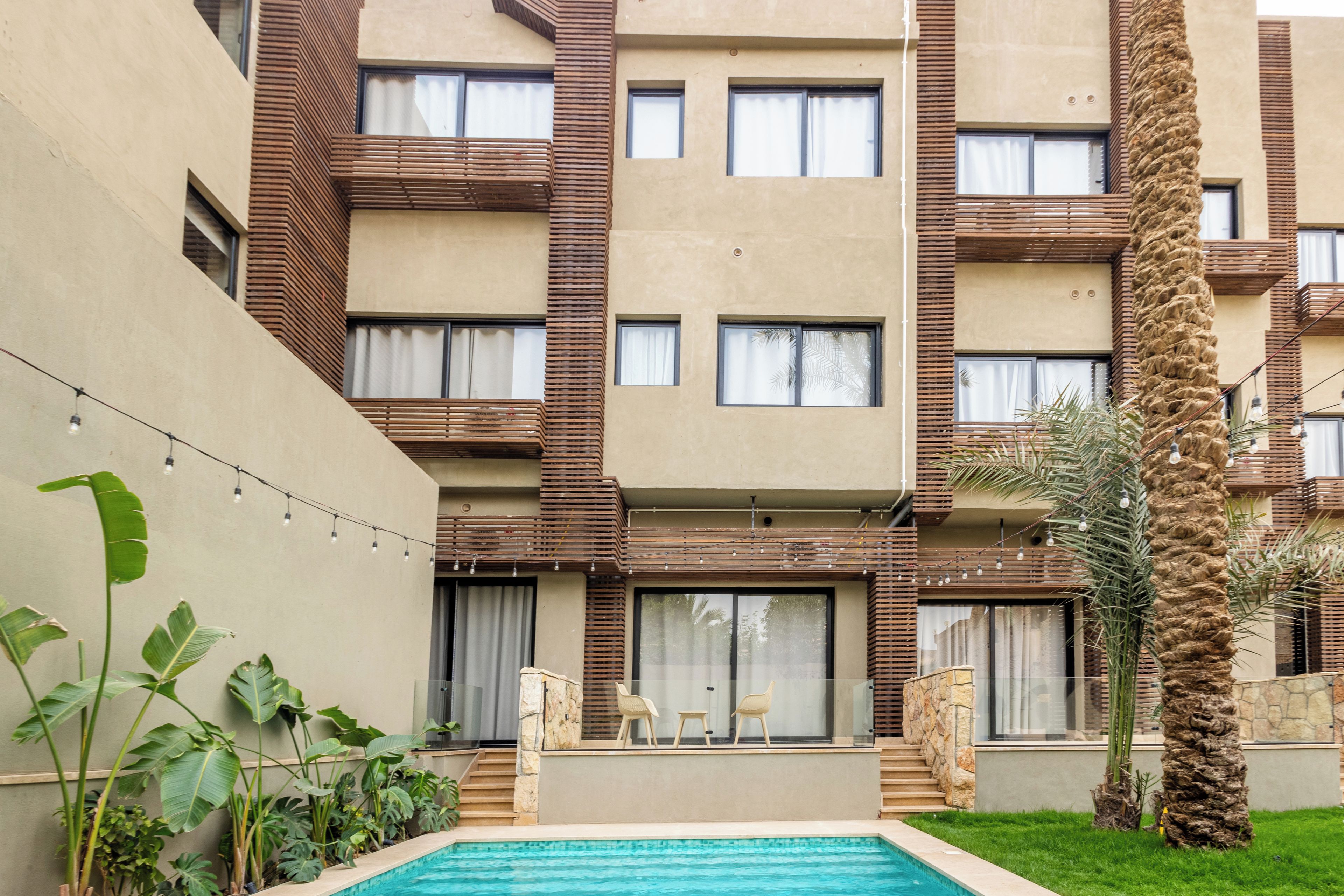 Um edifício moderno com piscina, área de estar externa e uma palmeira.