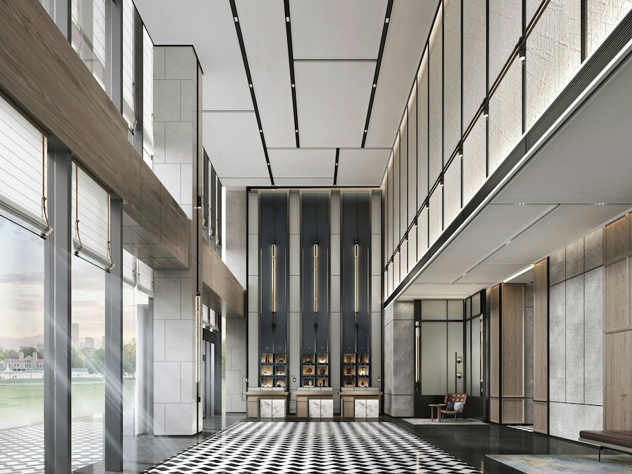 Um hall amplo com piso xadrez, janelas grandes e uma área de estar central com um banco e uma cadeira.