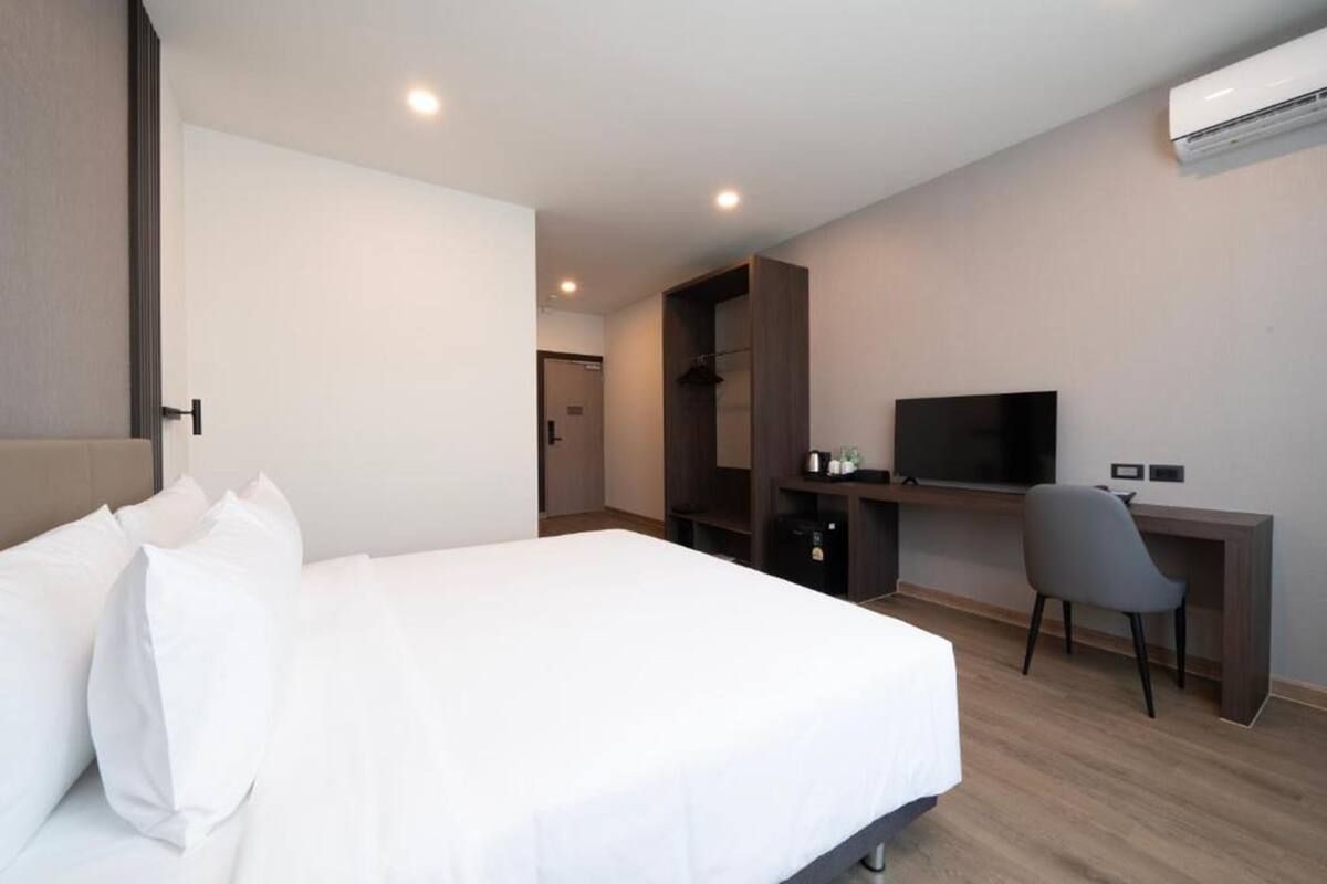 Quarto de hotel com uma cama, escrivaninha, televisão e guarda-roupa.