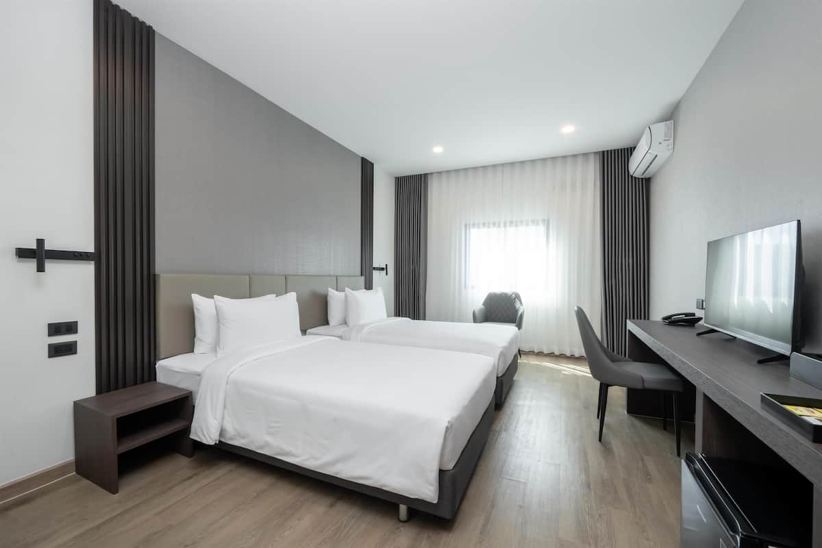 Quarto de hotel moderno com uma cama grande, uma escrivaninha, uma cadeira e uma televisão.