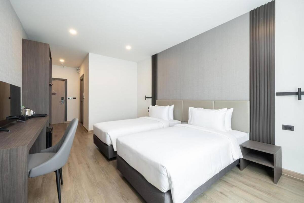 Quarto de hotel com duas camas, uma escrivaninha e uma cadeira.