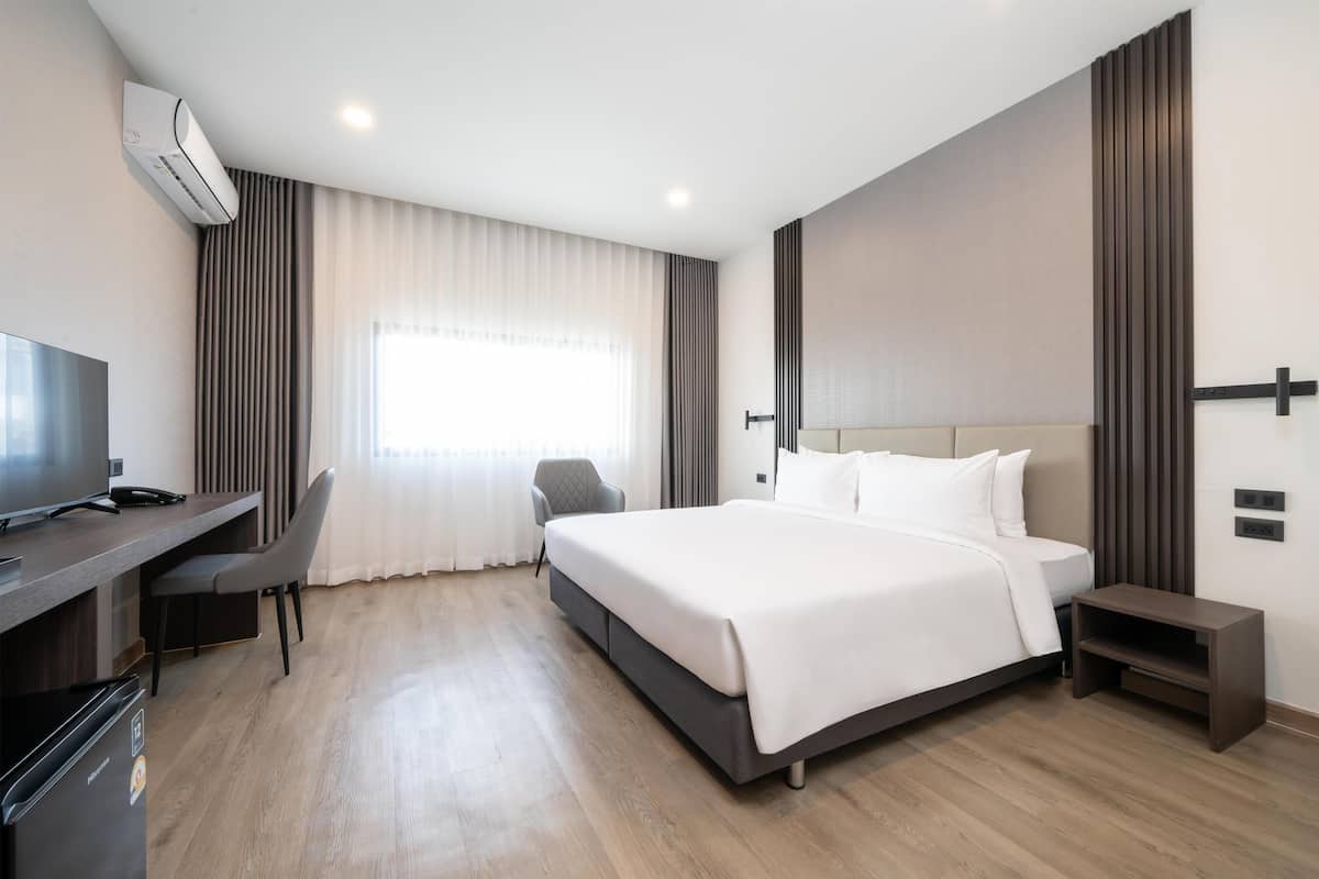 Quarto de hotel moderno com uma cama grande, uma escrivaninha com cadeira, uma televisão e ar condicionado instalado.