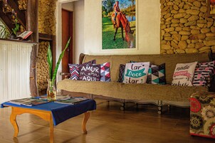 Uma sala de estar aconchegante com um banco de madeira decorado com almofadas coloridas, uma mesa de madeira com uma revista e uma parede de pedra ao fundo.