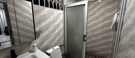 Um banheiro com parede estampada em mármore, pia branca, vaso sanitário e chuveiro com box de vidro.