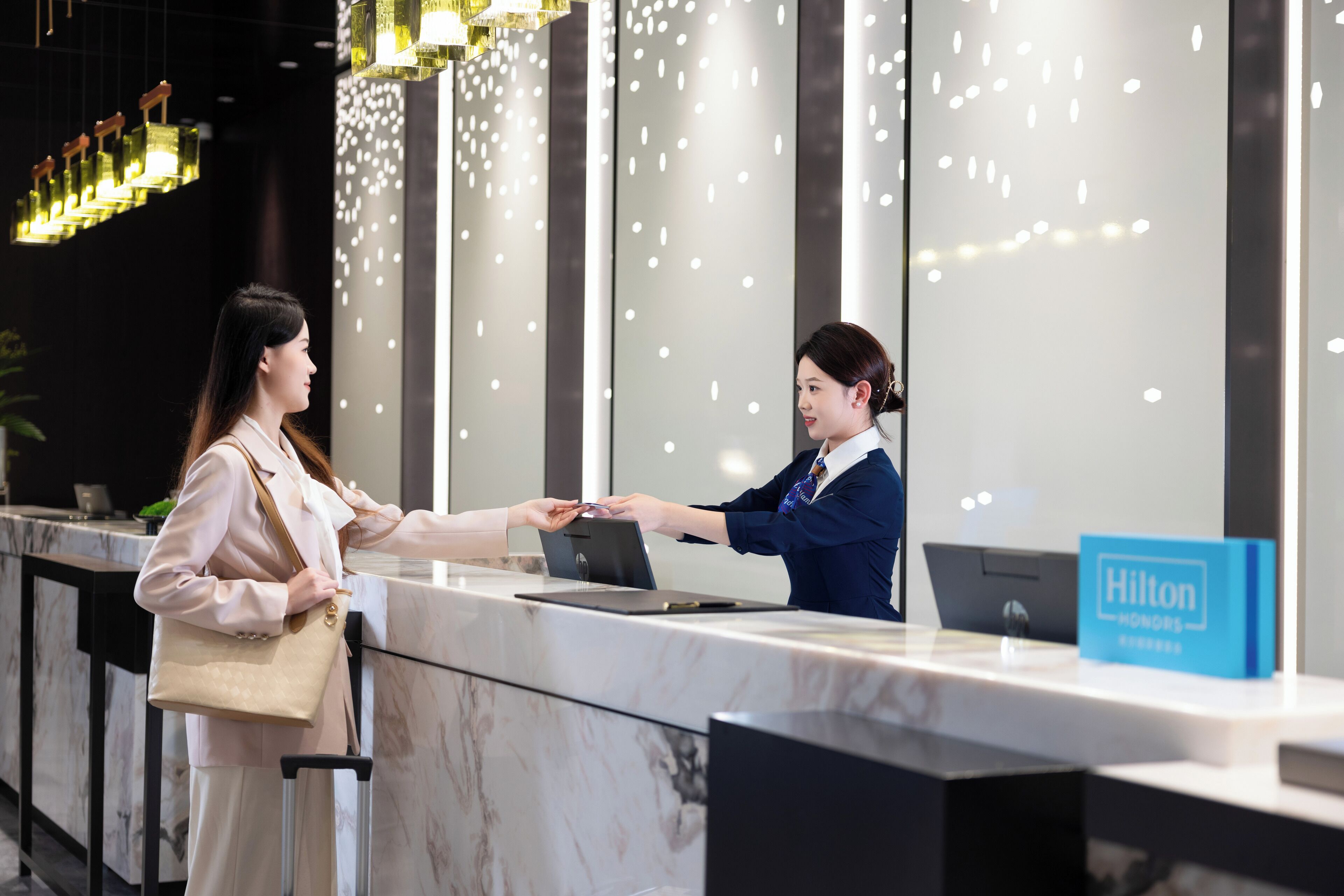 Balcão de recepção de hotel com design moderno, estação de check-in digital e placa indicando ser um hotel Hilton Honors.