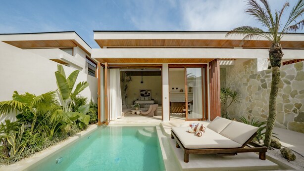 Uma área de piscina moderna ao ar livre, com espreguiçadeira e plantas tropicais.