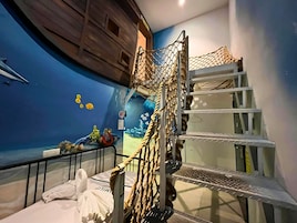 Um quarto com beliche, escada de corda e um mural de um naufrágio.