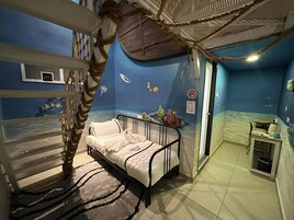 Quarto de criança com cama beliche, pequena escrivaninha e painel decorativo com tema de fundo marinho.