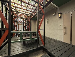 Uma área de estar coberta ao ar livre, com deck de madeira e estrutura metálica.