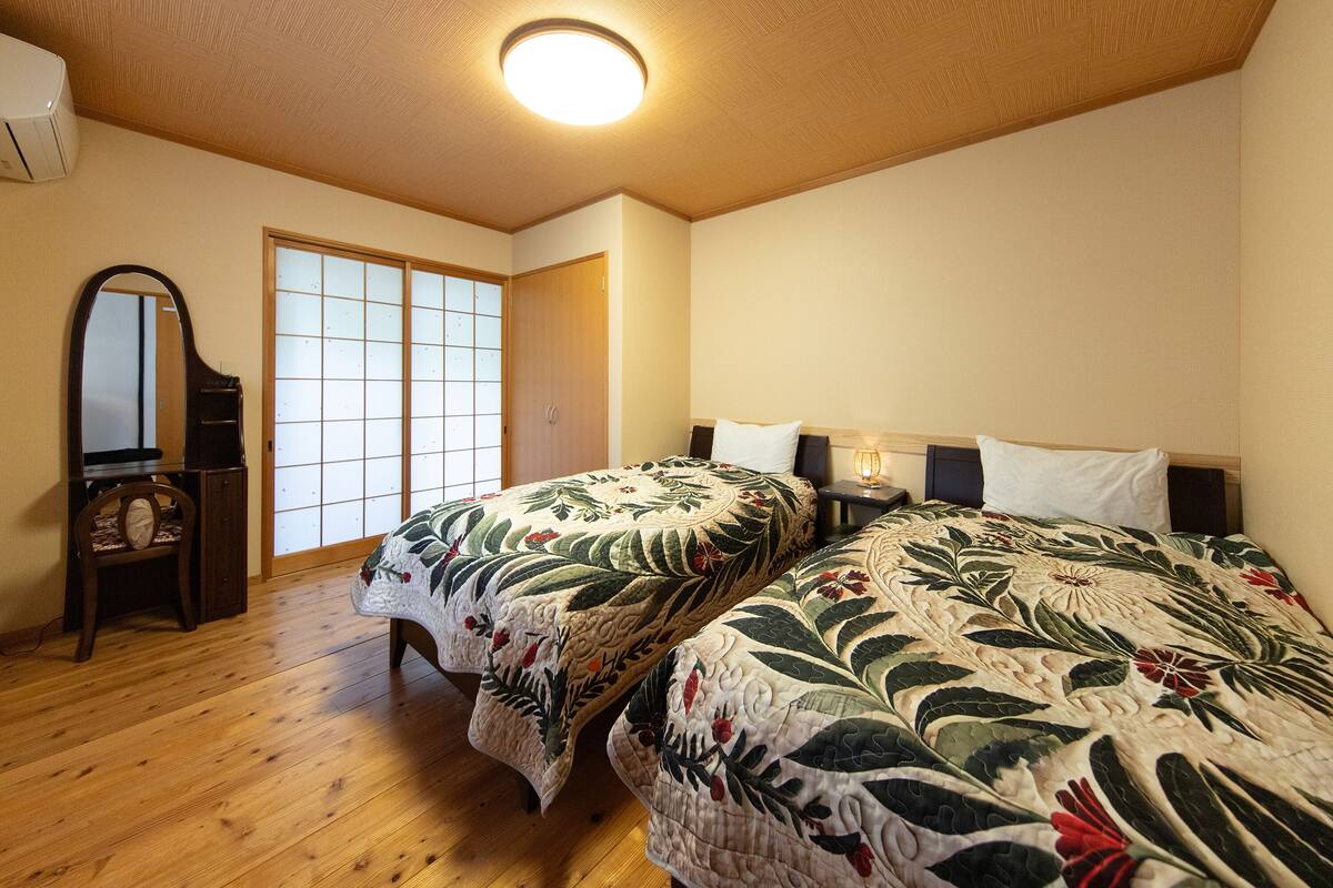 Quarto com duas camas, teto de madeira, um espelho e uma porta de correr.