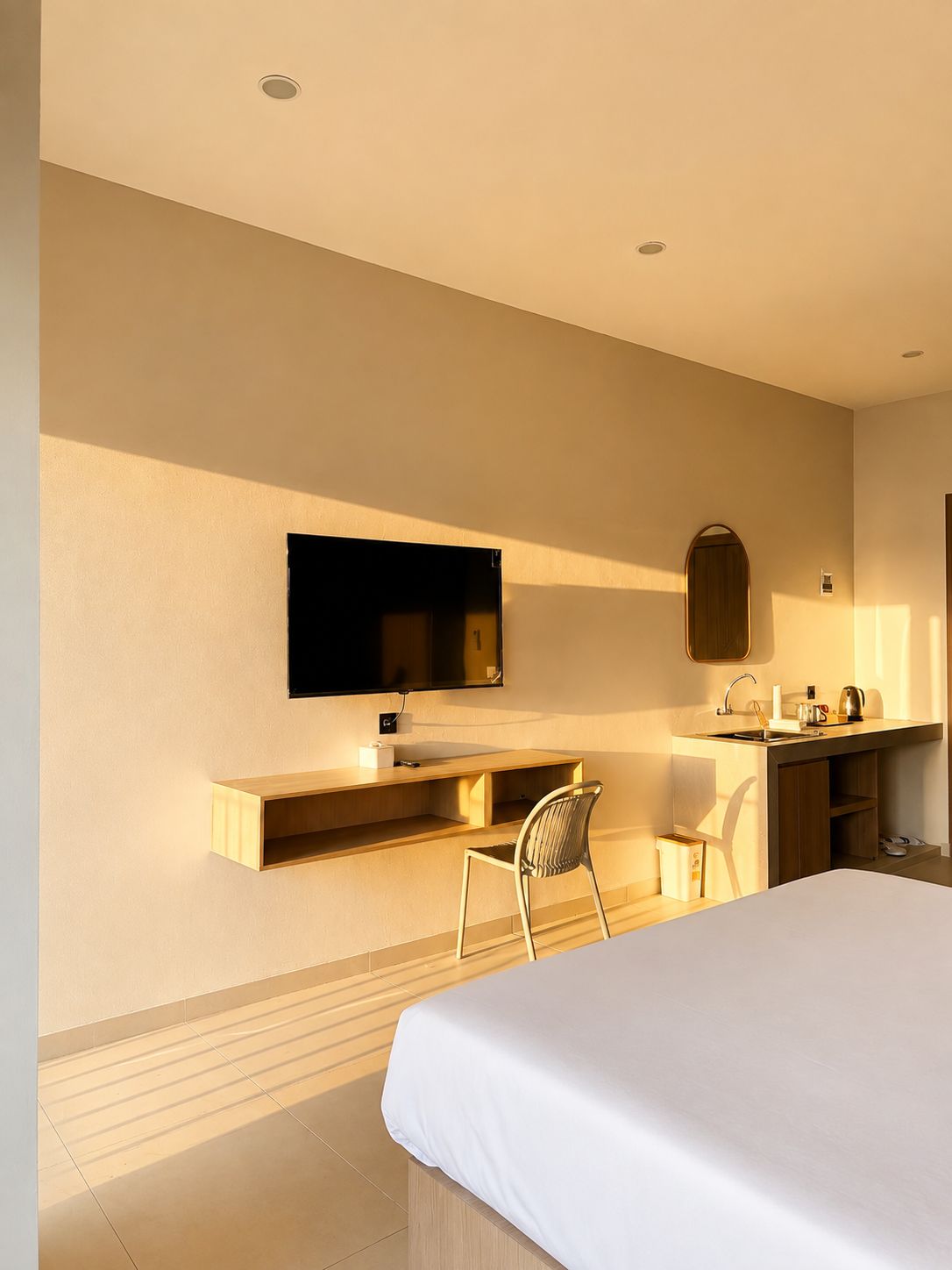 Quarto de hotel com cama, televisão fixada na parede, pequena escrivaninha com cadeira e pia embutida.