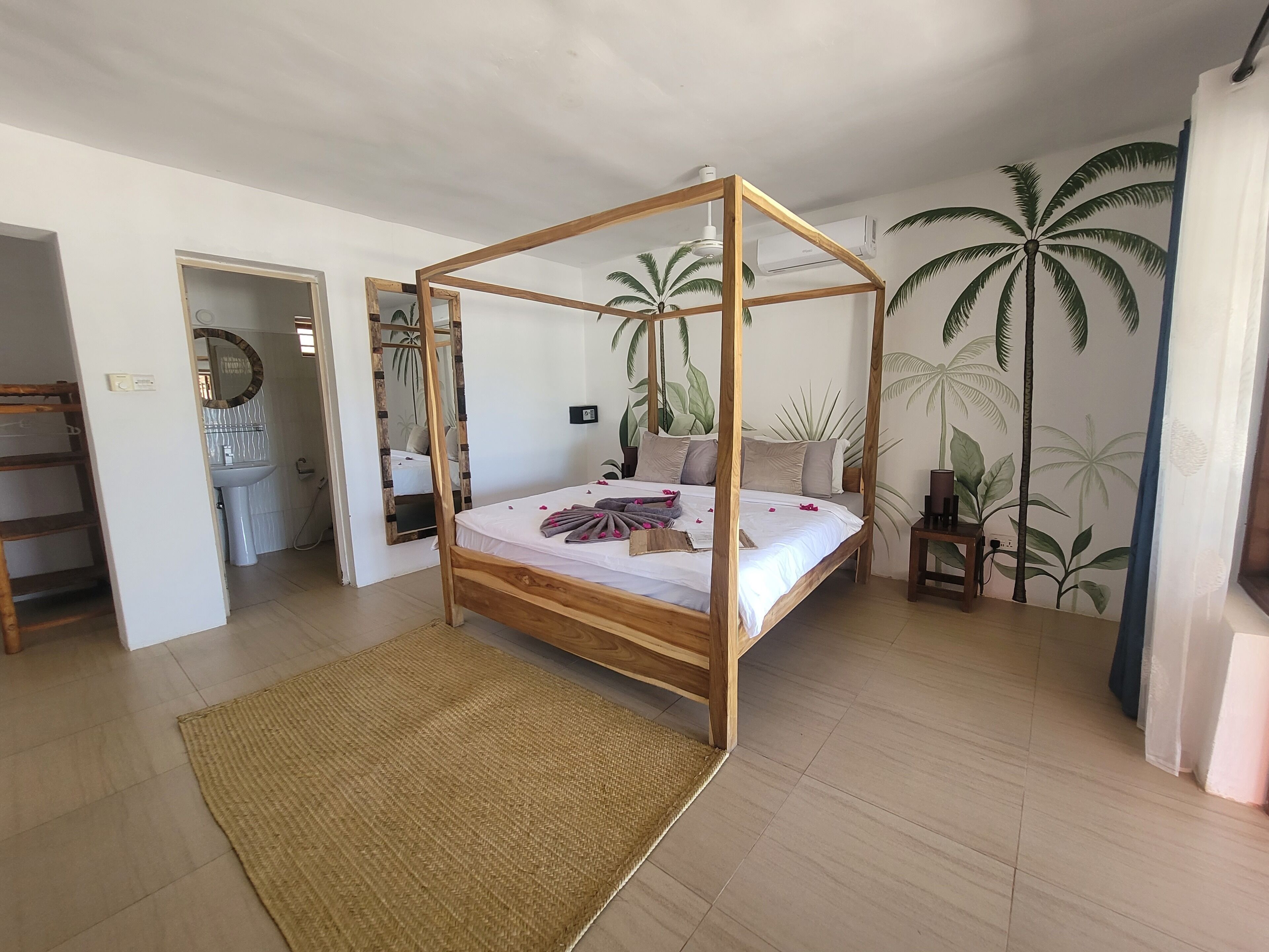 Quarto com cama de dossel, banheiro com pia e espelho, e uma planta grande.