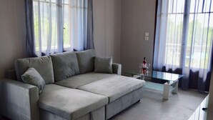 Uma sala de estar moderna com um sofá cinza, uma mesa de centro de vidro e uma garrafa de vinho.