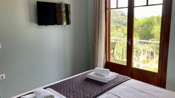 Quarto de hotel com uma cama, uma televisão na parede e uma janela com vista para áreas verdes.