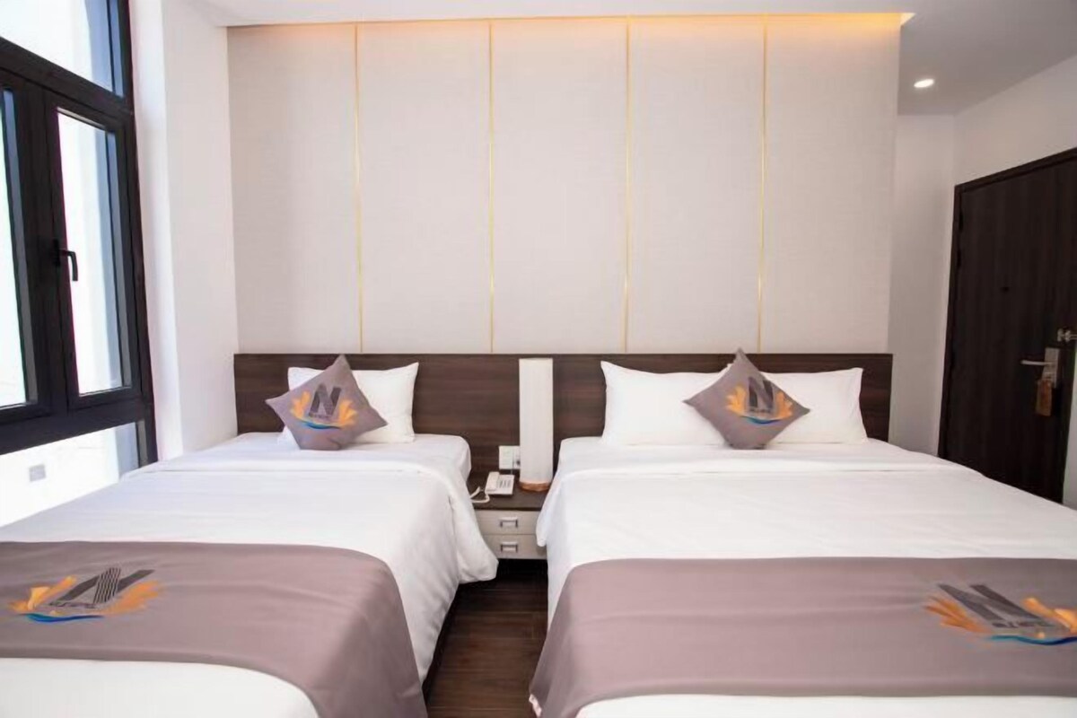 Quarto de hotel com duas camas, uma mesa de cabeceira, um telefone fixado na parede e uma janela.