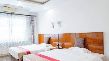 Quarto de hotel com duas camas, piso de madeira, uma janela grande com cortinas e luminária fixada na parede.