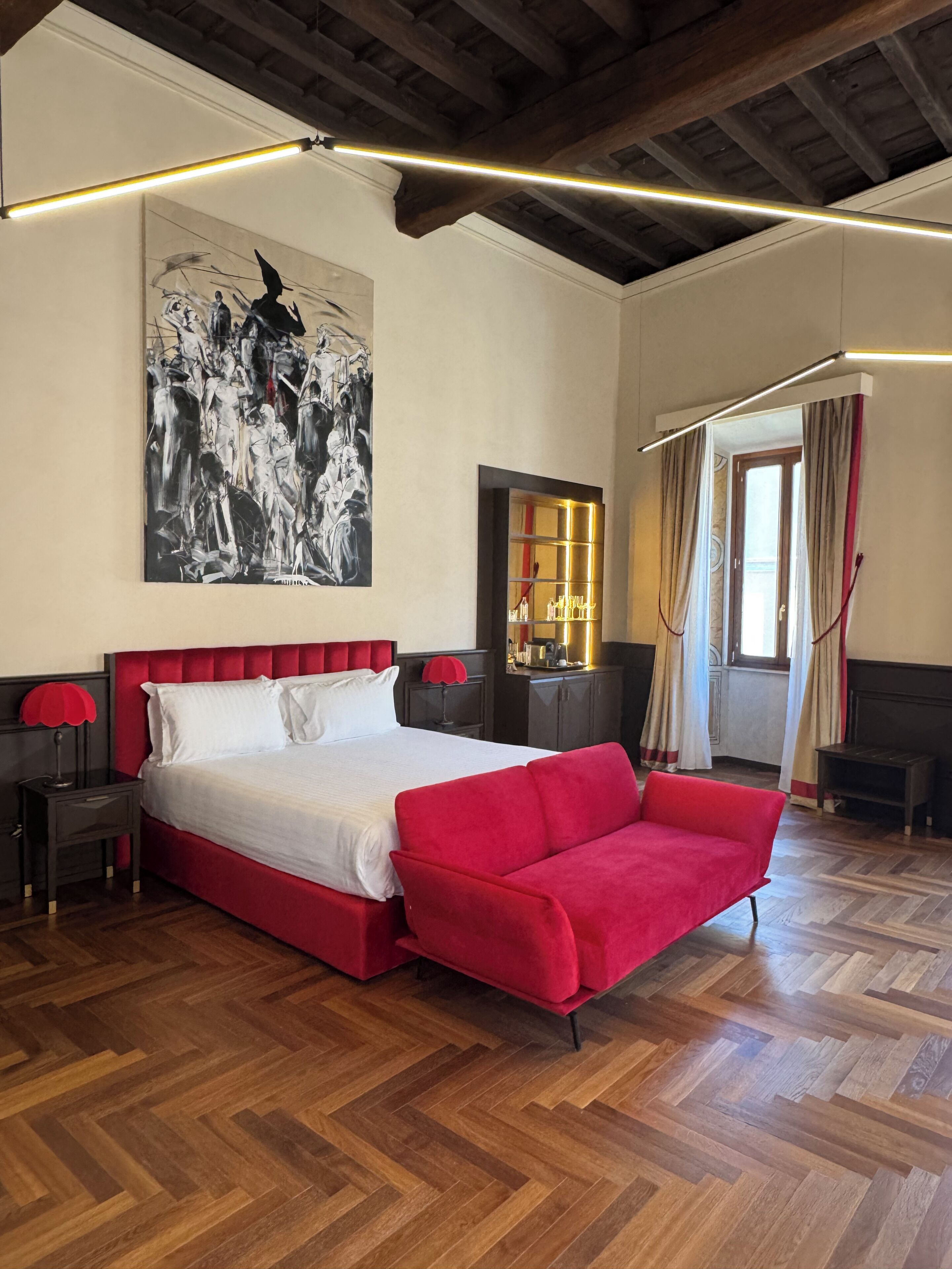Quarto com uma cama grande, um sofá vermelho, um quadro na parede e teto de madeira.