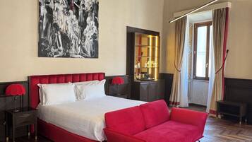 Quarto com uma cama grande, um sofá vermelho, um quadro na parede e teto de madeira.