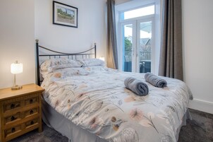 Cama bem arrumada com roupa de cama florida, luminária de cabeceira e mesa de cabeceira de madeira com gavetas.