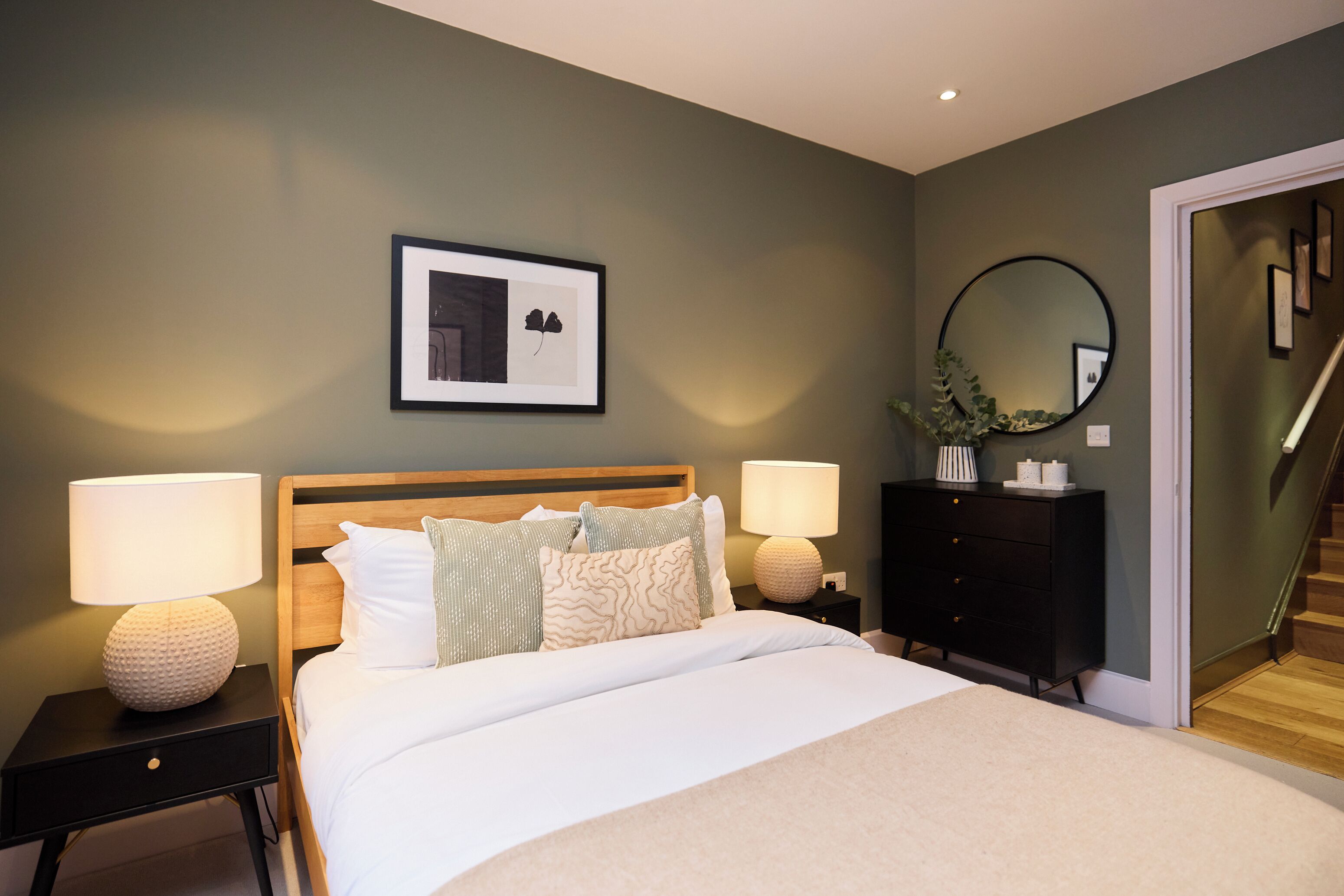 Quarto com cama, duas mesas de cabeceira com abajures, cômoda, espelho e um quadro na parede.
