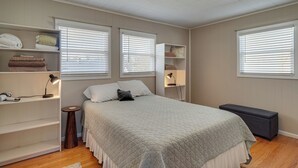 Quarto com cama, estantes embutidas, um banco e uma pequena mesa com abajur.