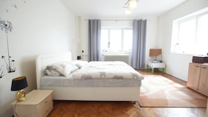 Quarto com cama, mesa de cabeceira, abajur e vista para o exterior.