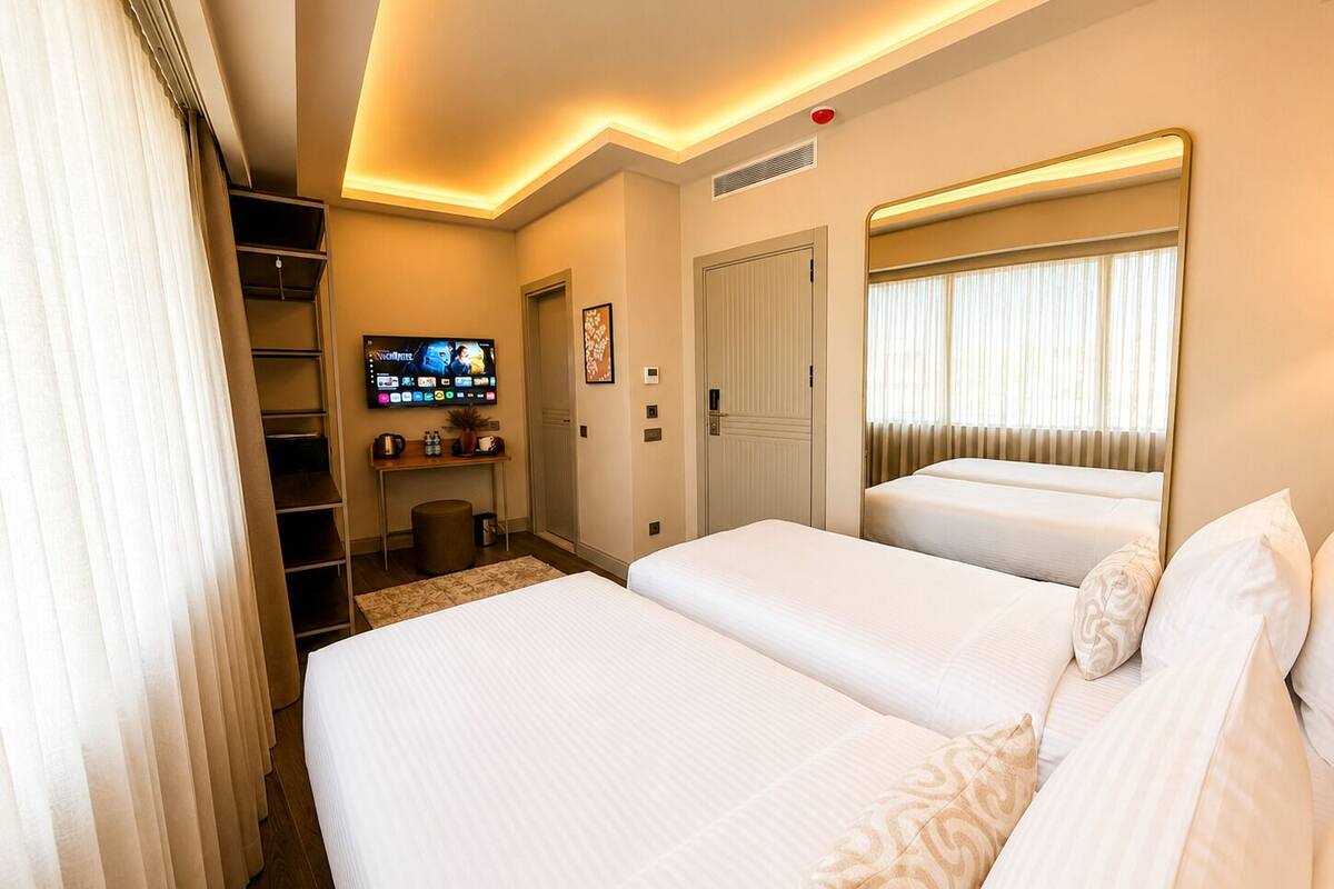 Quarto de hotel com duas camas, uma televisão, uma mesa com cafeteira e uma porta.