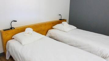 Quarto de hotel com duas camas de solteiro, cada uma com cabeceira de madeira e roupa de cama branca.
