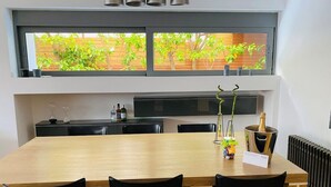 Uma área de refeições moderna com uma grande mesa de madeira, cadeiras pretas, uma pequena planta e uma garrafa de champanhe.