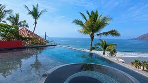Uma piscina infinita com vista para o oceano e a praia, rodeada por palmeiras e uma estrutura com telhado de palha.