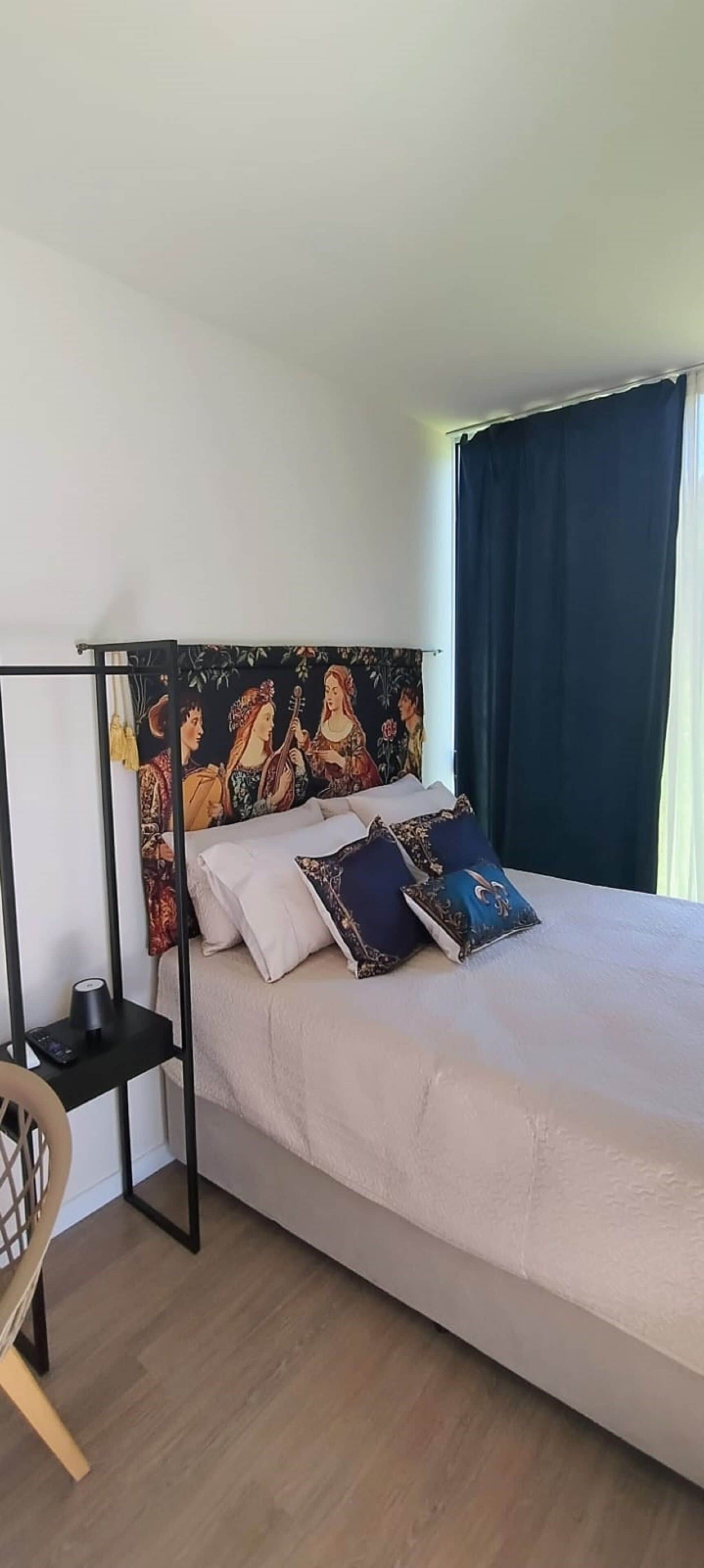 Uma cama com cabeceira, travesseiros, mesa de cabeceira e uma cadeira.